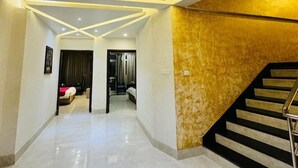 Um hall de hotel espaçoso com design moderno, destacando um piso de mármore e uma escadaria com detalhes dourados.