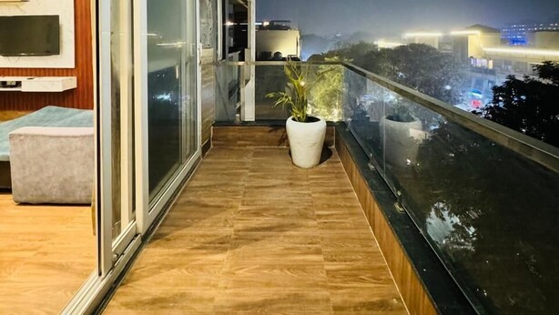 Uma varanda com piso de madeira, um vaso com planta e vista da cidade à noite.