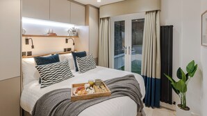 Quarto de hotel moderno com uma cama grande, mesas de cabeceira, bandeja de café da manhã e vista para o exterior.