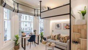 Uma sala de estar moderna com um sofá, uma mesa de centro, uma área de refeições com uma cadeira e uma estante de livros.