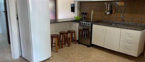 Cozinha compacta com geladeira, fogão e banquetas de bar.