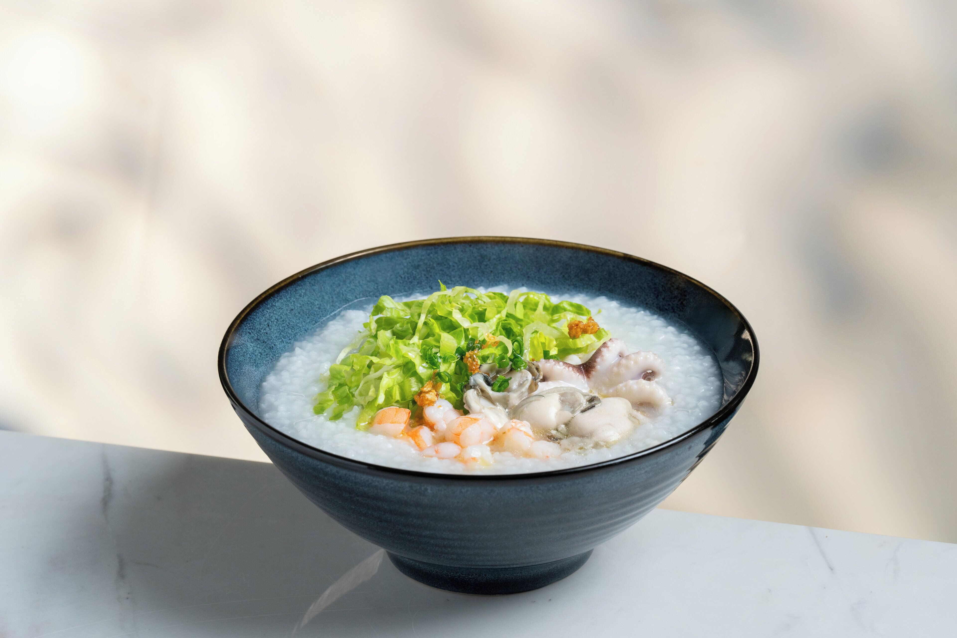 Uma tigela de mingau de frutos do mar com cobertura verde, colocada sobre uma superfície de mármore.