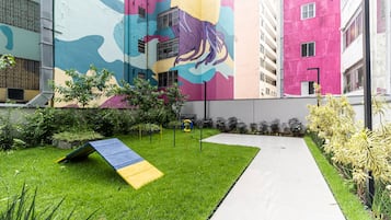 Um pátio com área gramada, um caminho e um mural colorido em um edifício.