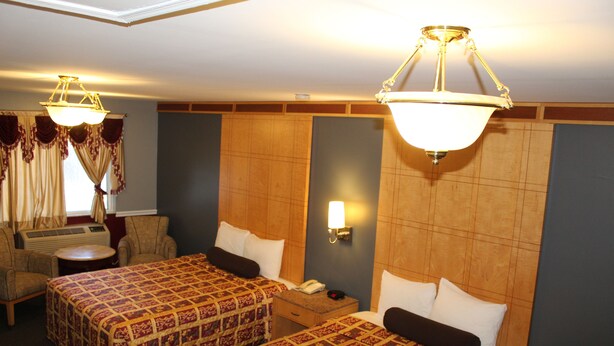 Quarto de hotel com duas camas, um espaço de estar com uma poltrona e uma mesa, um telefone fixado na parede e um lustre no teto.