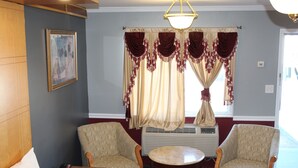 Quarto com duas poltronas estofadas, uma mesa redonda pequena, um telefone e um quadro na parede.