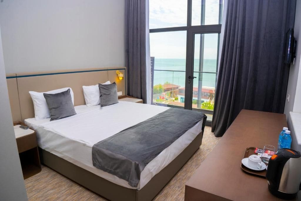 Quarto de hotel com uma cama grande, uma escrivaninha, uma cadeira, televisão e vista para o mar.