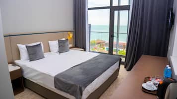 Quarto de hotel com uma cama grande, uma escrivaninha, uma cadeira, televisão e vista para o mar.
