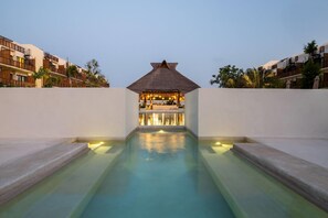Piscina com área de bar no centro, rodeada por edifícios com varandas.