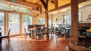 Restaurante com vigas de madeira, janelas amplas e piso ladrilhado.