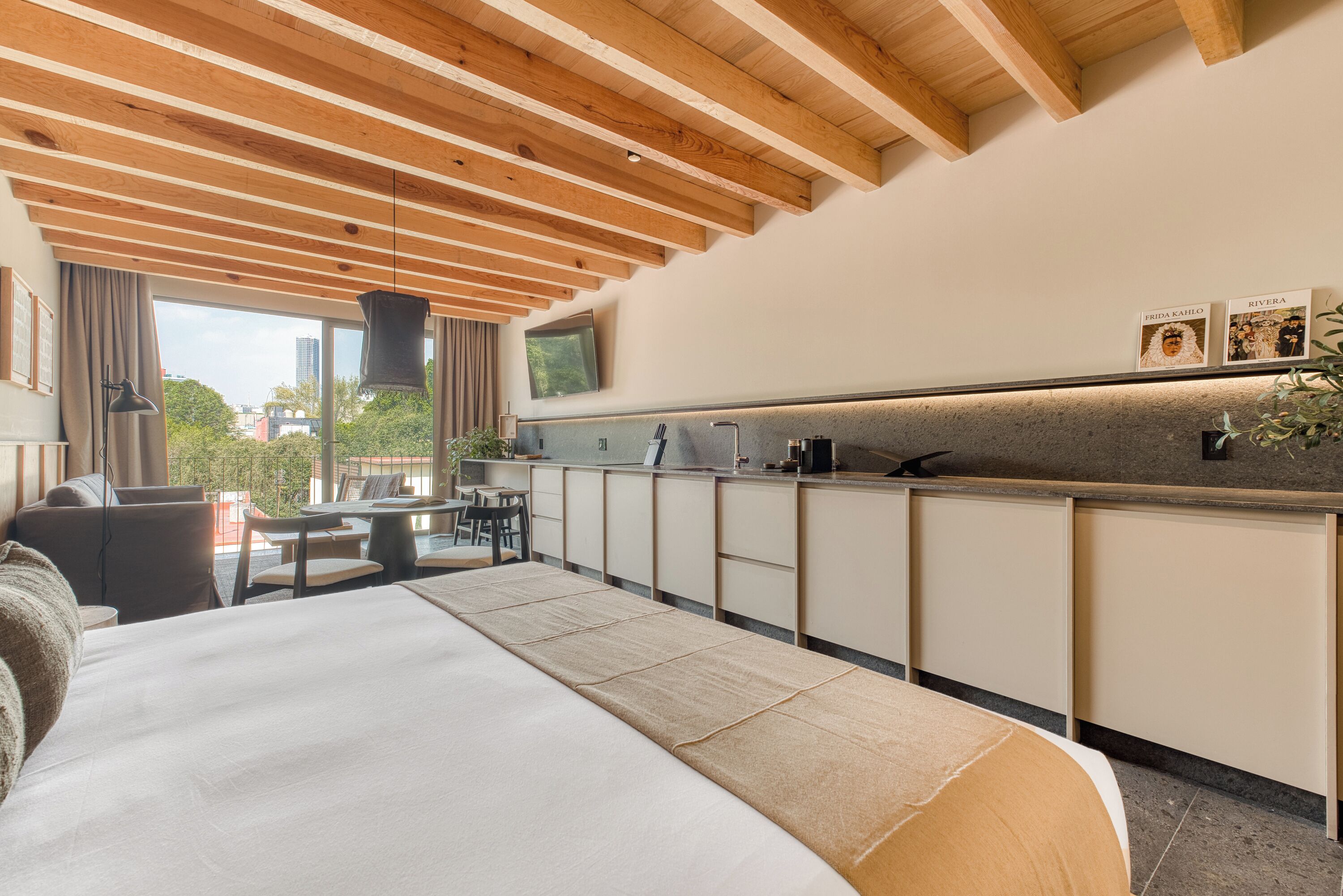 Quarto de hotel moderno com uma cama grande, cozinha compacta, área de refeições e vista para a cidade.