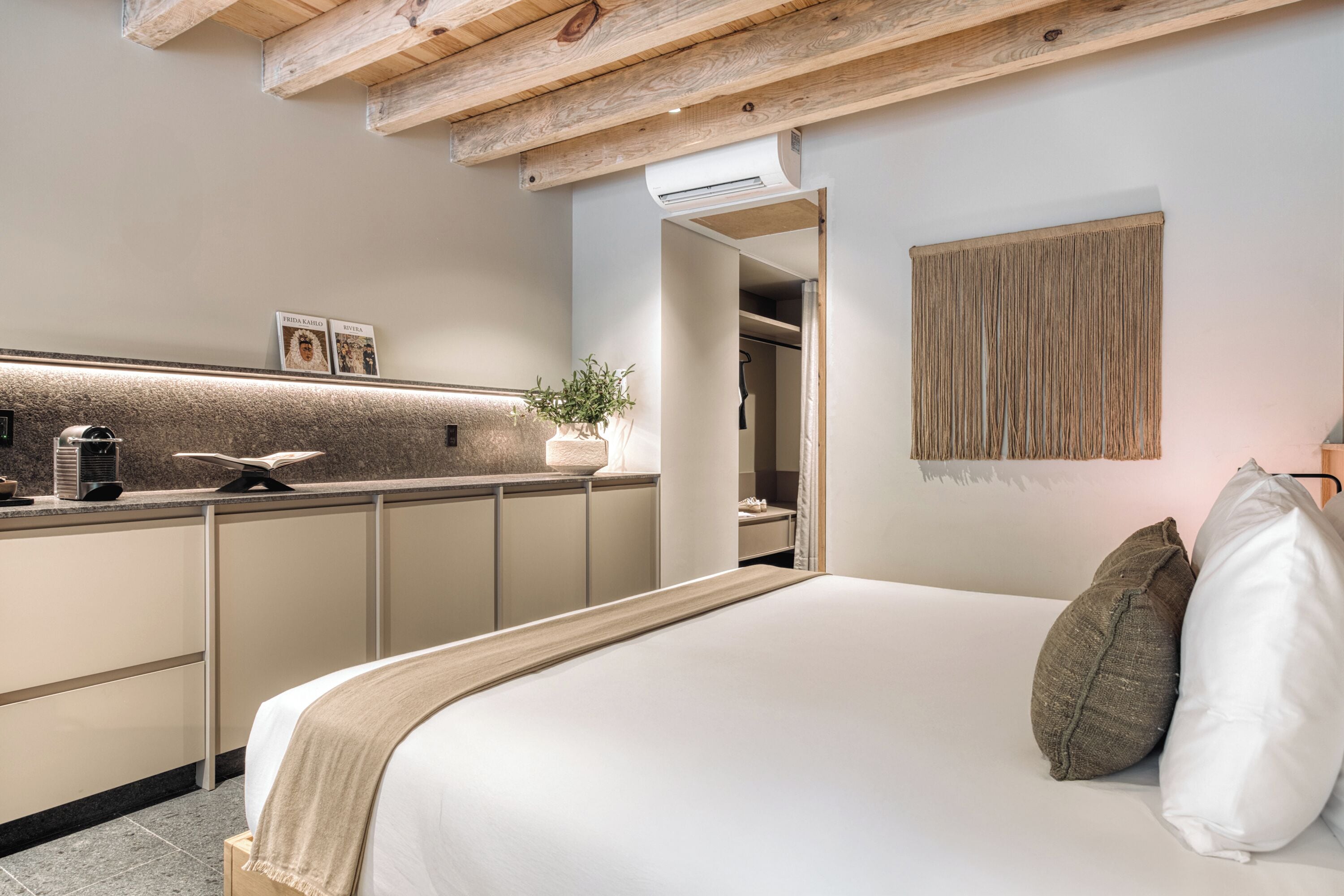Quarto com cama, mesa de cabeceira e criado-mudo. Há uma janela com vista para o exterior.
