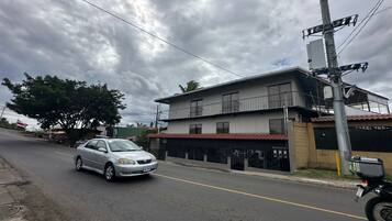 Vista da rua com um prédio de dois andares, um carro estacionado e uma motocicleta.