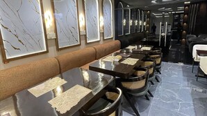 Um restaurante moderno com arte em parede de mármore, iluminação embutida e uma extensa área de jantar com cabines e mesas.