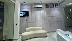 Uma área de recepção moderna com piso de mármore, painel de parede em madeira e uma televisão instalada.