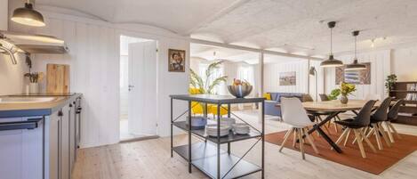 Cozinha espaçosa com ilha central, área de jantar com mesa redonda e cadeiras, e sala de estar com sofá e mesa de centro.