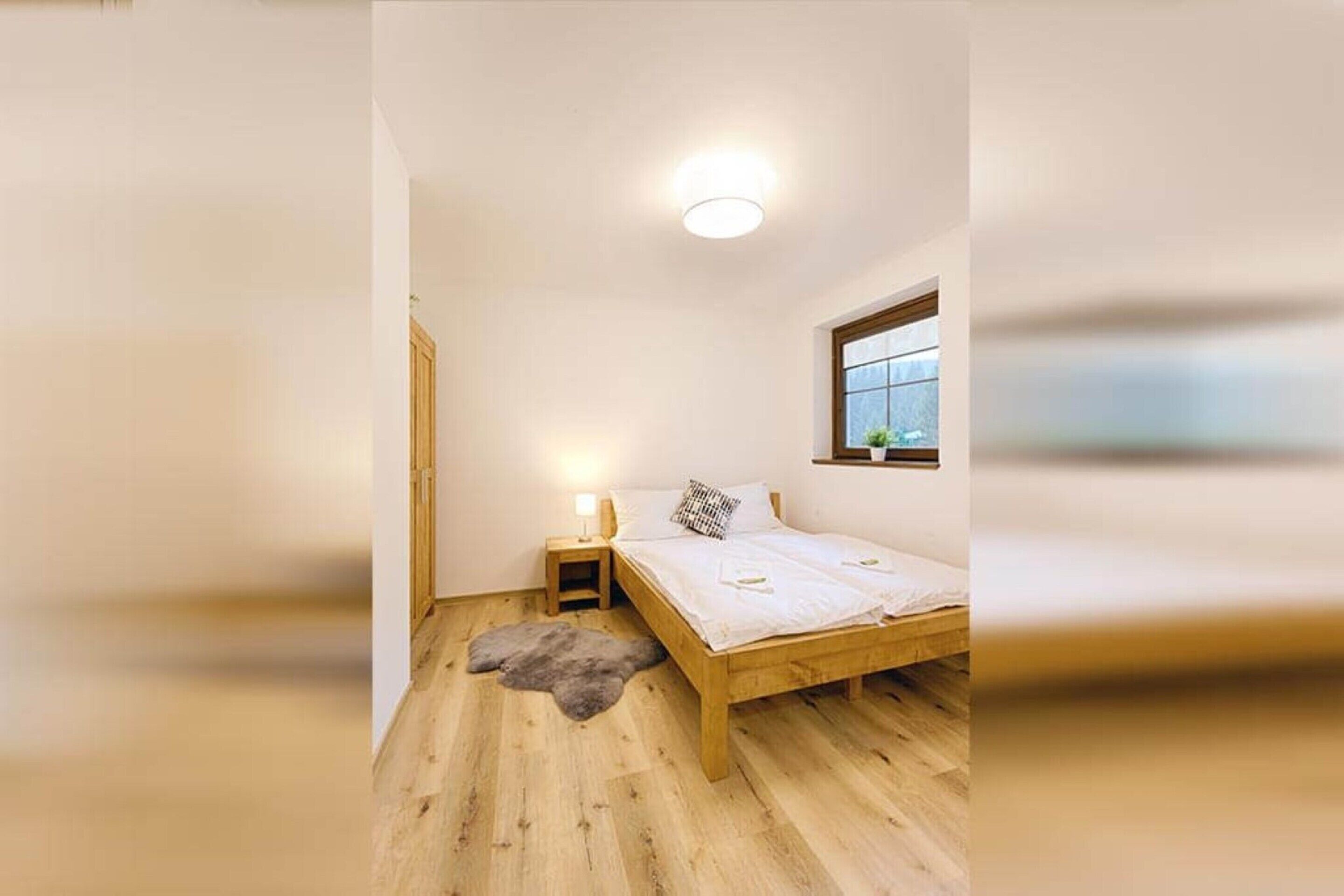 Quarto com cama de madeira, mesa de cabeceira com abajur, janela e tapete de pele no chão.