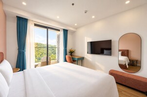 Quarto de hotel com cama, escrivaninha, cadeira, televisão e varanda com vista.