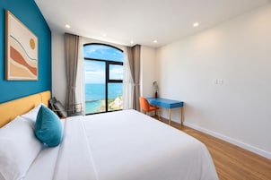 Quarto de hotel com uma cama grande, uma escrivaninha e vista para o mar.