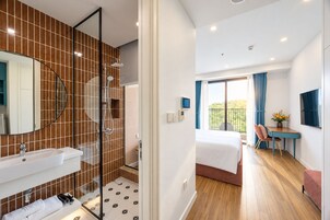 Quarto de hotel com banheiro, uma cama, escrivaninha e vista para o exterior.