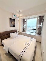Quarto de hotel com cama, mesa de cabeceira, janela com cortinas e ar condicionado fixado na parede.