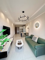 Sala de estar moderna com sofá verde, mesa de centro branca, televisão e área de jantar ao fundo.