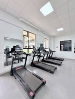 Academia com várias esteiras, amplas janelas e interior limpo e claro.
