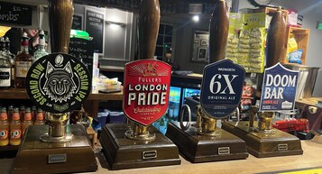 Um bar com quatro torneiras de cerveja identificadas como 'WADWORTH 6X', 'DOOM BAR', 'FULLER'S LONDON PRIDE' e 'WOLFPACK'.