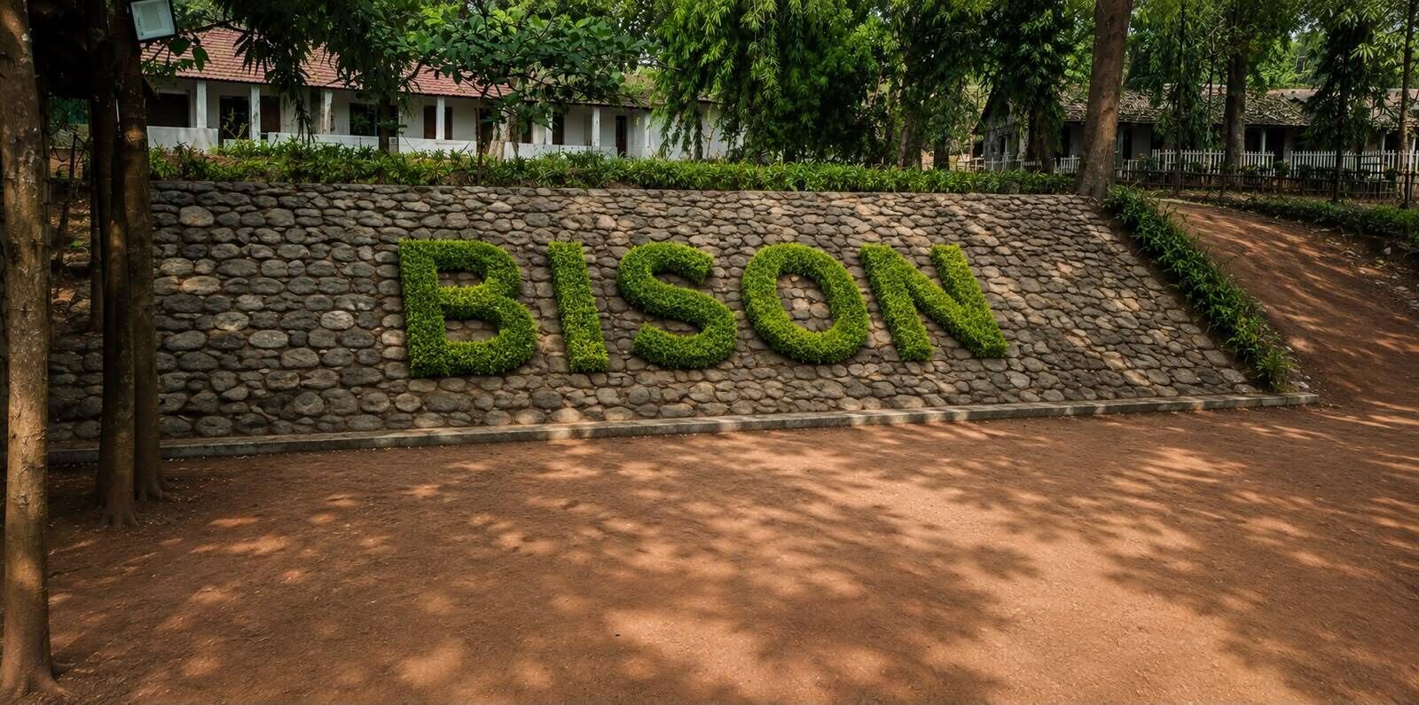 Um muro de pedra com a palavra 'BISON' formada por vegetação, cercado por árvores e um caminho de terra.