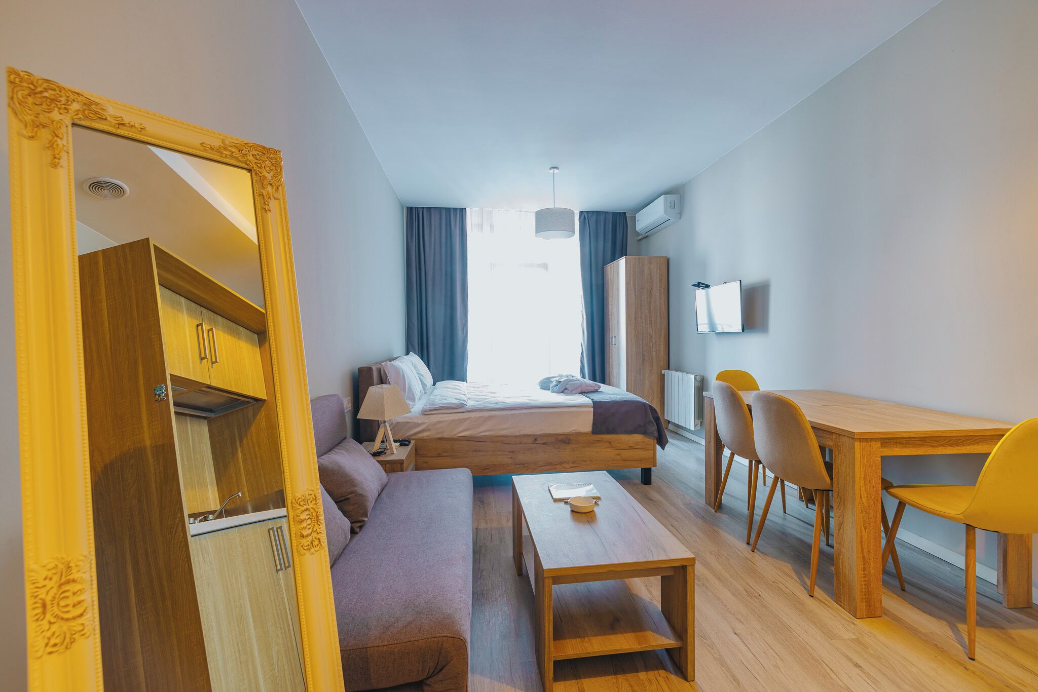 Quarto de hotel moderno com cama, sofá, mesa de jantar e espelho.
