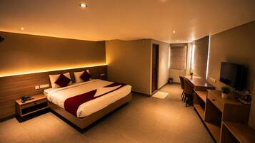 Quarto de hotel moderno com uma cama grande, mesa de cabeceira, escrivaninha e televisão.