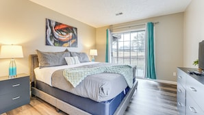 Um quarto com uma cama, mesas de cabeceira, cômoda, janela com cortinas e um quadro na parede.