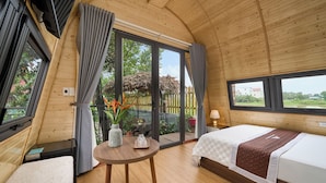 Quarto aconchegante com cama, mesa com vaso e bandeja, e uma janela grande com cortinas.