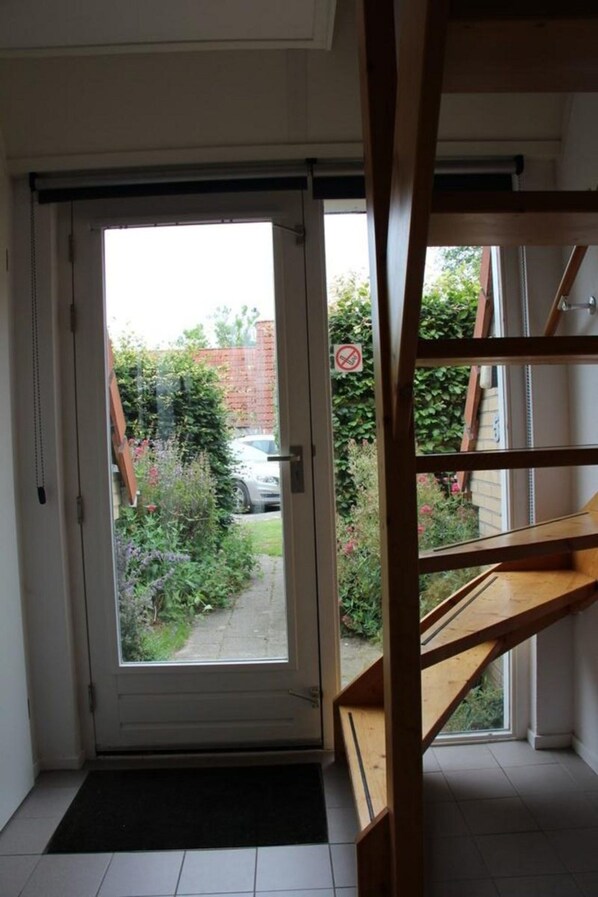 Quarto com porta para um jardim, escada de madeira e tapete de entrada.