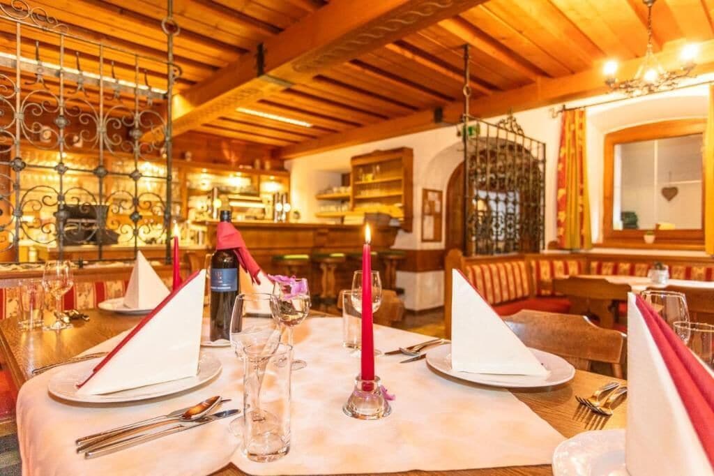 Restaurante com vigas de madeira, mesas iluminadas por velas e um bar ao fundo.