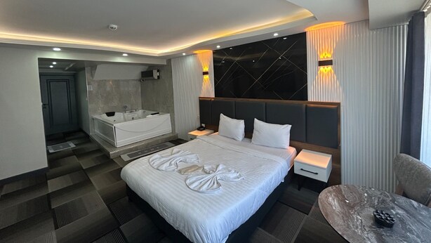 Quarto de hotel moderno com uma cama grande, banheiro separado com banheira, área de estar com mesa e vista para a cidade.