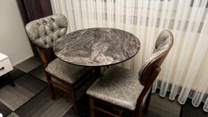 Uma mesa redonda com tampo de mármore, duas cadeiras estofadas com estrutura de madeira, uma escrivaninha branca e um tapete listrado.