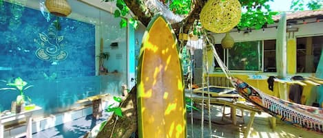 Quarto com uma grande janela, uma rede, uma árvore e uma prancha de surf.