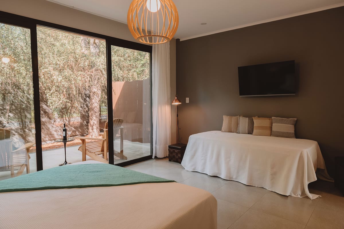 Quarto com cama, televisão, janela com vista para árvores e cadeira perto da janela.