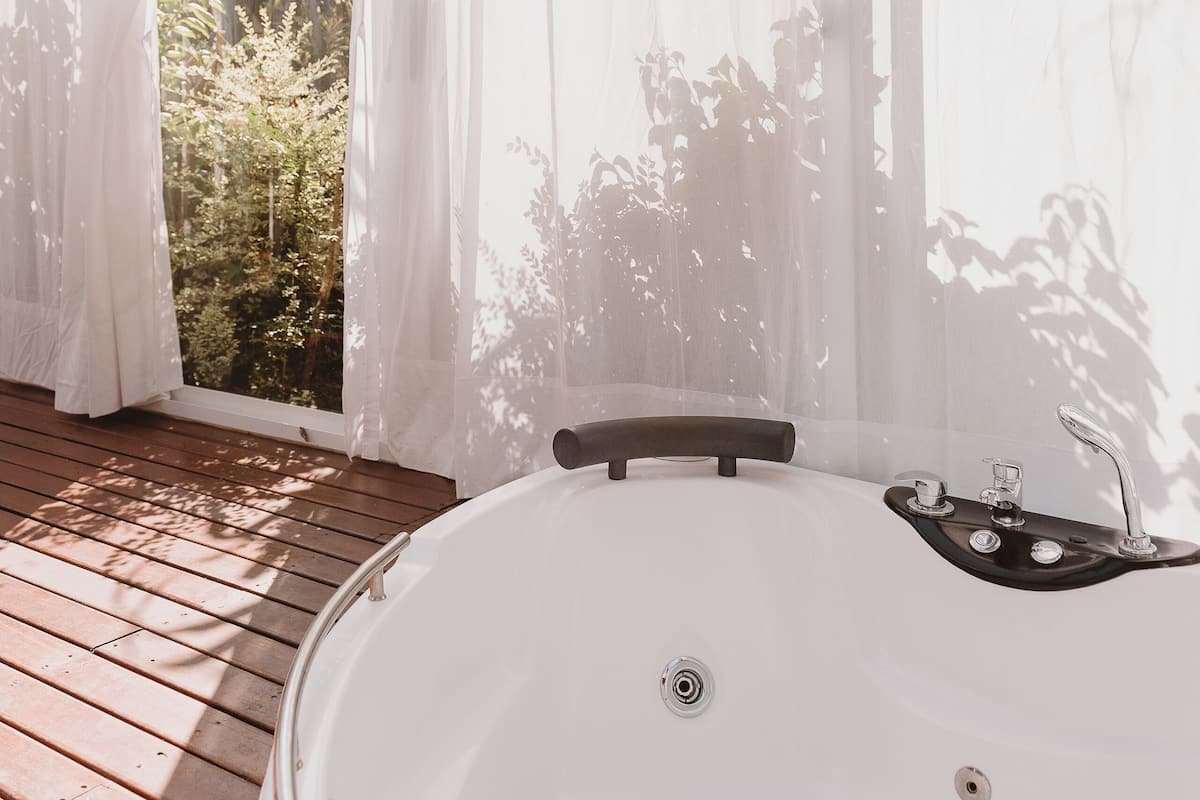 Área de spa com hidromassagem, deck de madeira e cortinas leves.