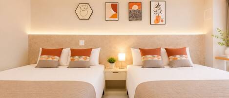 Quarto de hotel com duas camas, uma mesa de cabeceira, um abajur e quatro obras de arte emolduradas na parede.