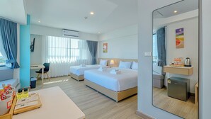 Quarto de hotel com duas camas, uma escrivaninha, uma cadeira, um pequeno espaço de cozinha e um banheiro.
