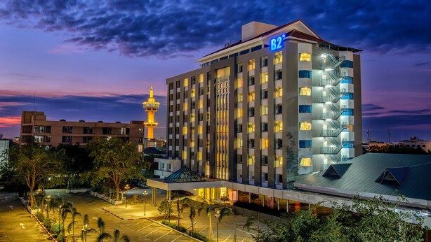 Um hotel de vários andares com uma placa de destaque 'B2', uma torre com pináculo iluminado e uma área de estacionamento com árvores.