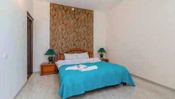 Quarto com cama de madeira, duas mesas de cabeceira com abajures, parede com padrão e piso em tons claros.