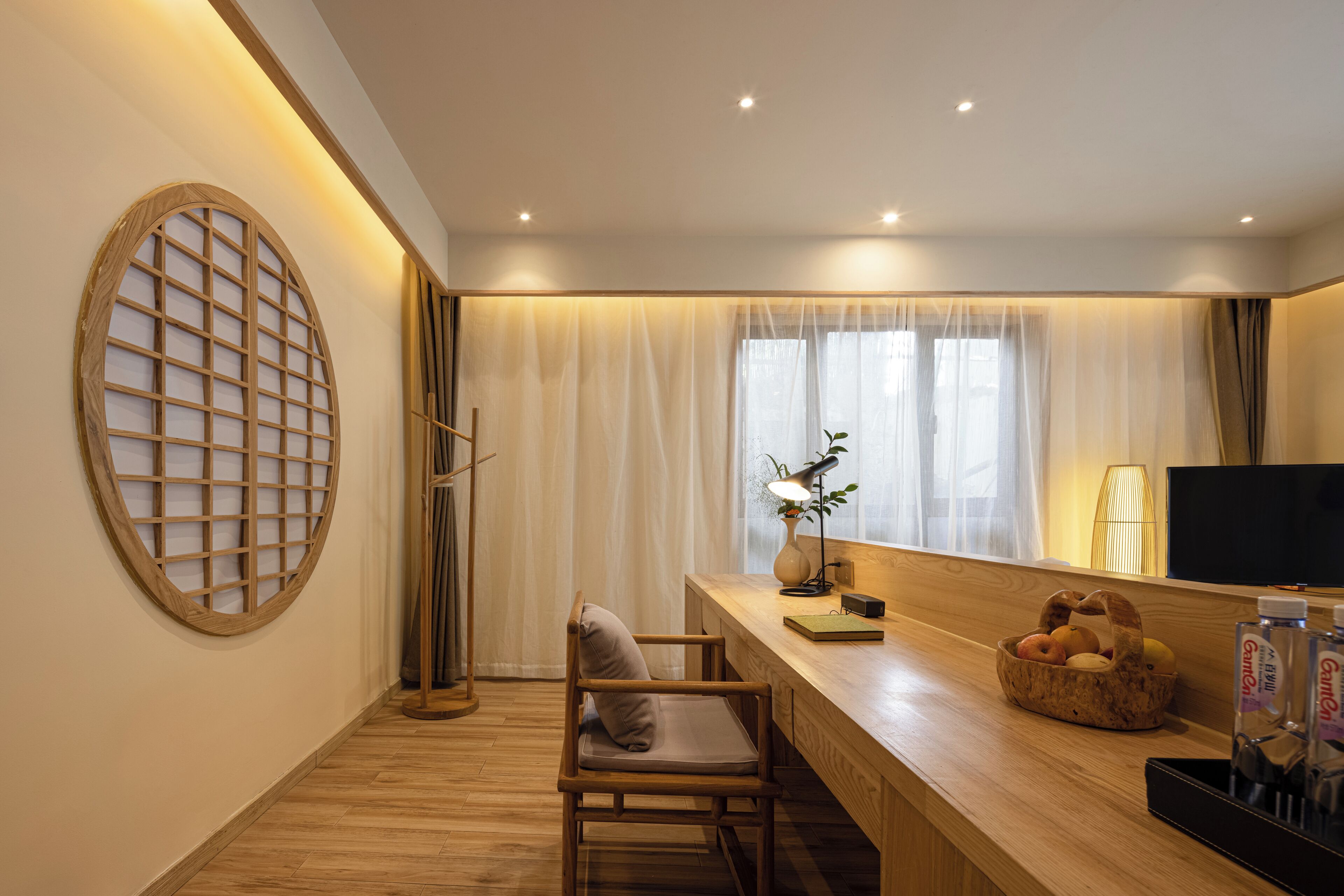 Quarto moderno com escrivaninha de madeira, uma cadeira, janela redonda, luminária e TV.