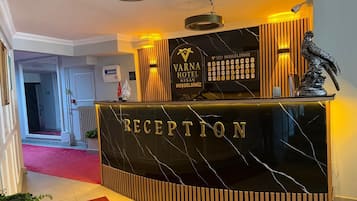 Bancada de recepção com tampo de mármore, placa com o nome do hotel e uma estátua de um pássaro.