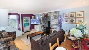 Uma sala de estar com lareira de pedra, uma televisão e um espaço de jantar com mesa e cadeiras.