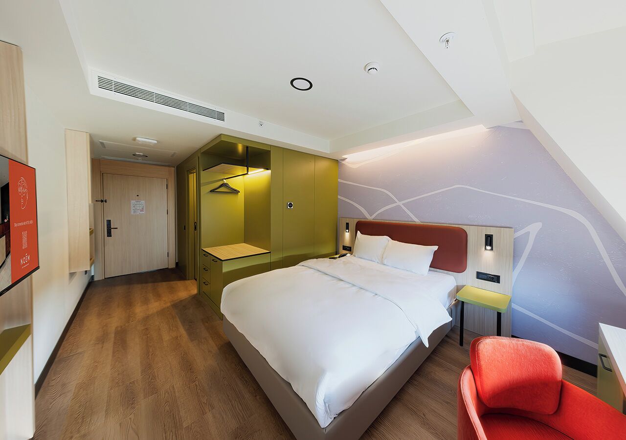 Quarto de hotel com cama, escrivaninha, cadeira e guarda-roupa.