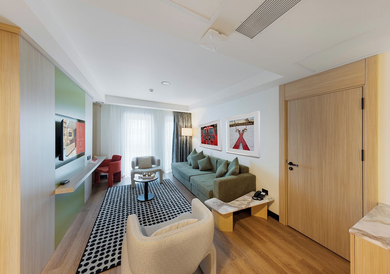 Quarto de hotel moderno com sofá, uma mesinha, uma cadeira, televisão e guarda-roupa.