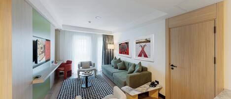 Quarto de hotel moderno com sofá, uma mesinha, uma cadeira, televisão e guarda-roupa.