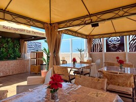 An outdoor restaurant with tables and chairs, a sign reading "Restaurant La Terrasse", and a view of the sky through large windows.
